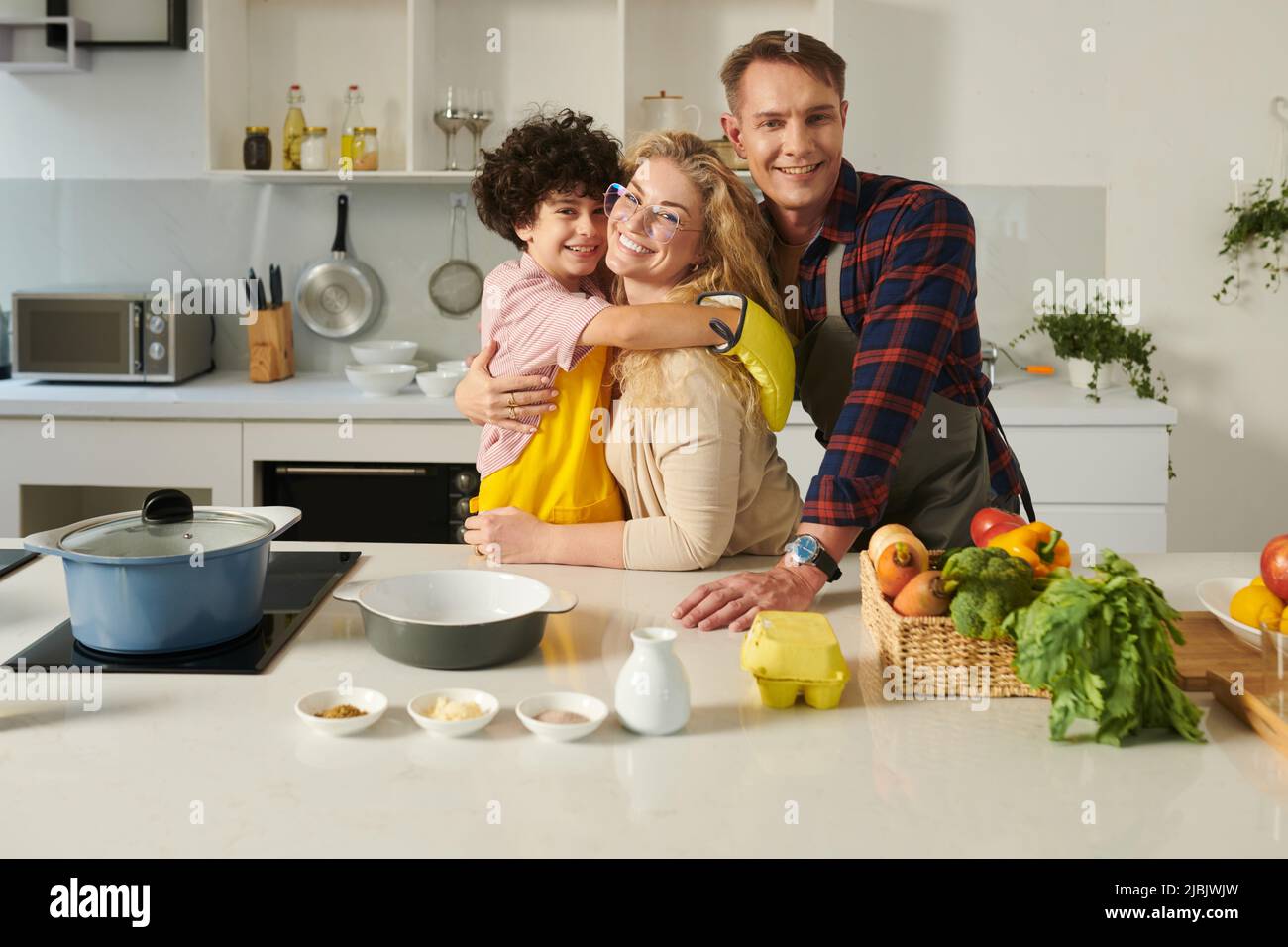 Happy family of three standing at kitchen counter, hugging and looking ...