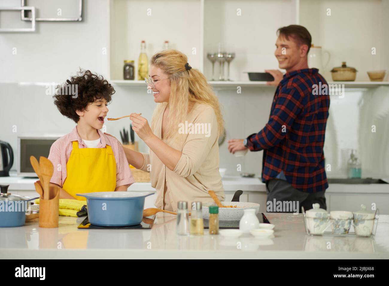 Smiling mother giving son some pasta sauce to taste for seasoning Stock ...