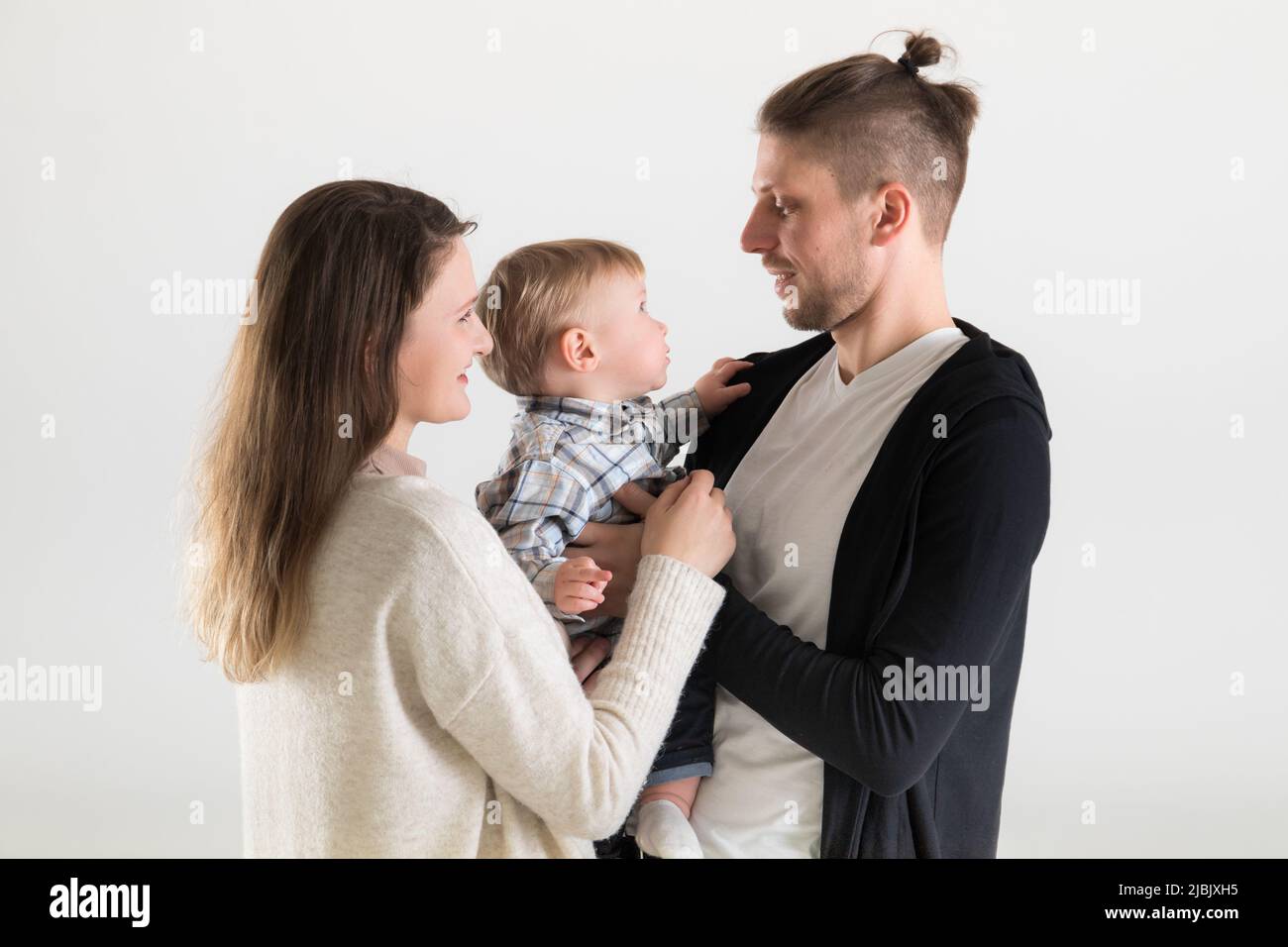 Young parents hold their child in their arms and look at him on a white ...