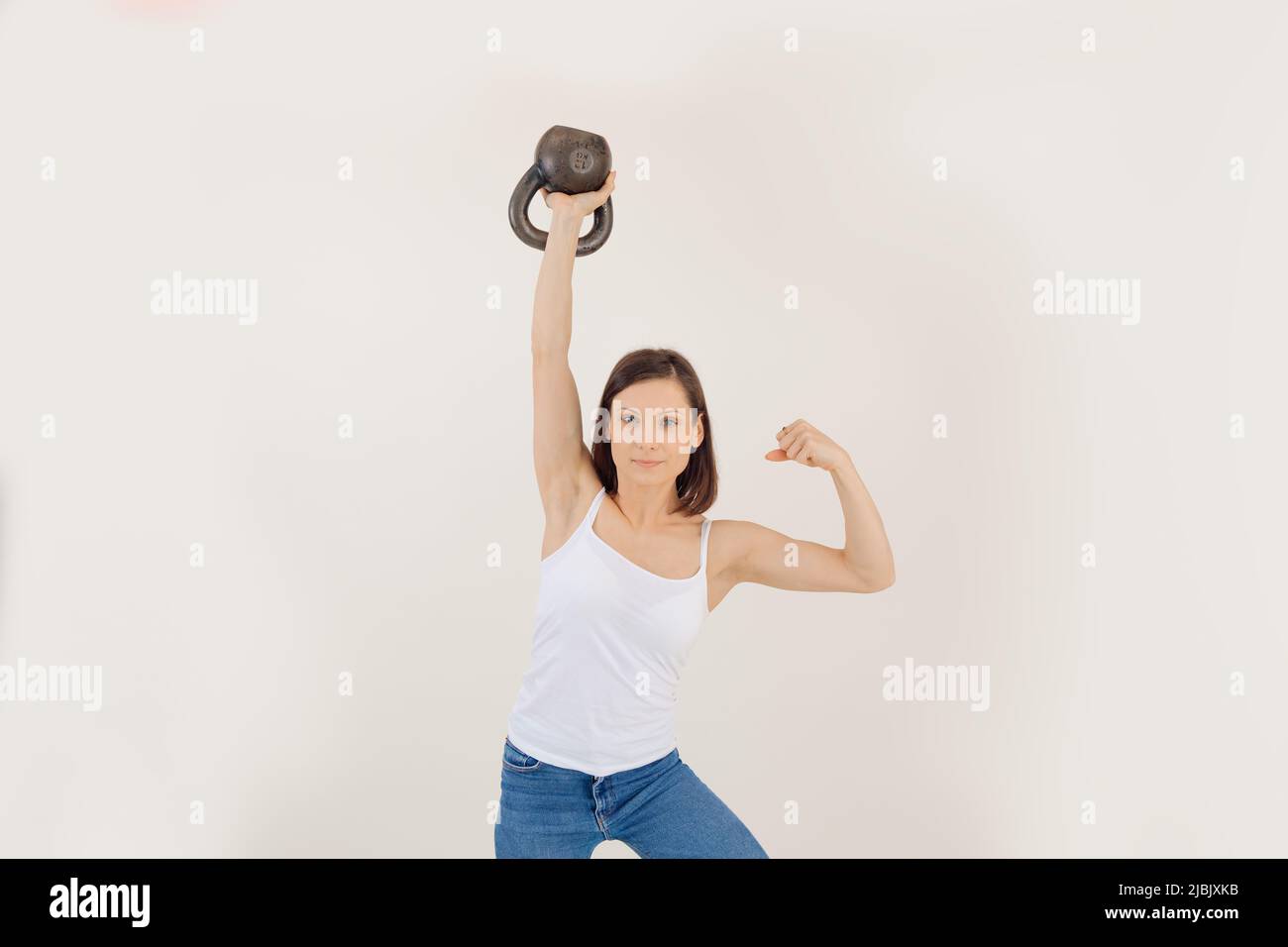 Young athletic woman lifting up kettlebell and straining muscles, white ...