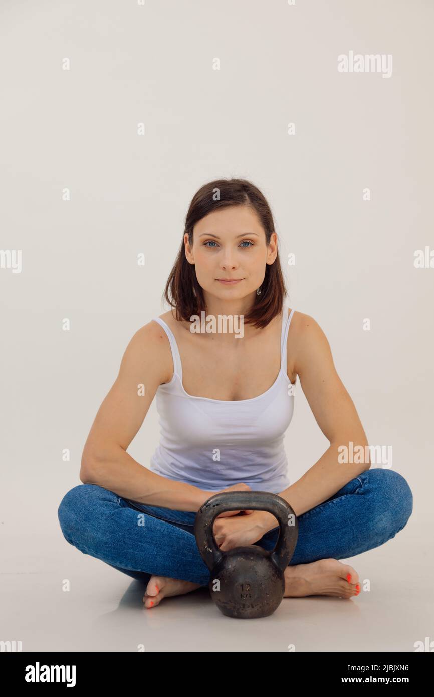 Young athletic woman sitting with kettlebell and straining muscles ...