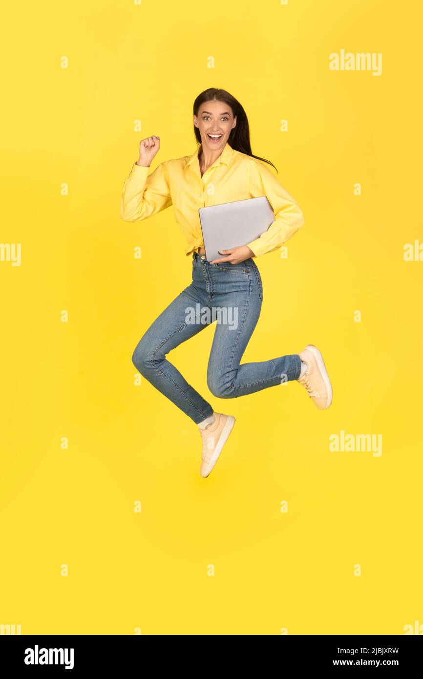 Joyful Lady Jumping Holding Laptop Shaking Fists Over Yellow Background ...