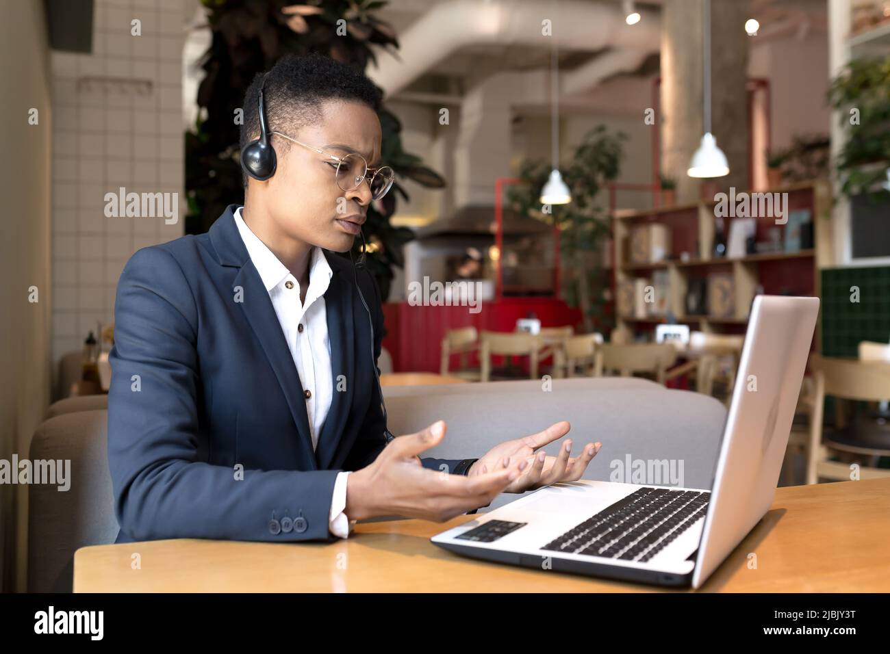Serious African American woman uses a headset for a video call, works ...
