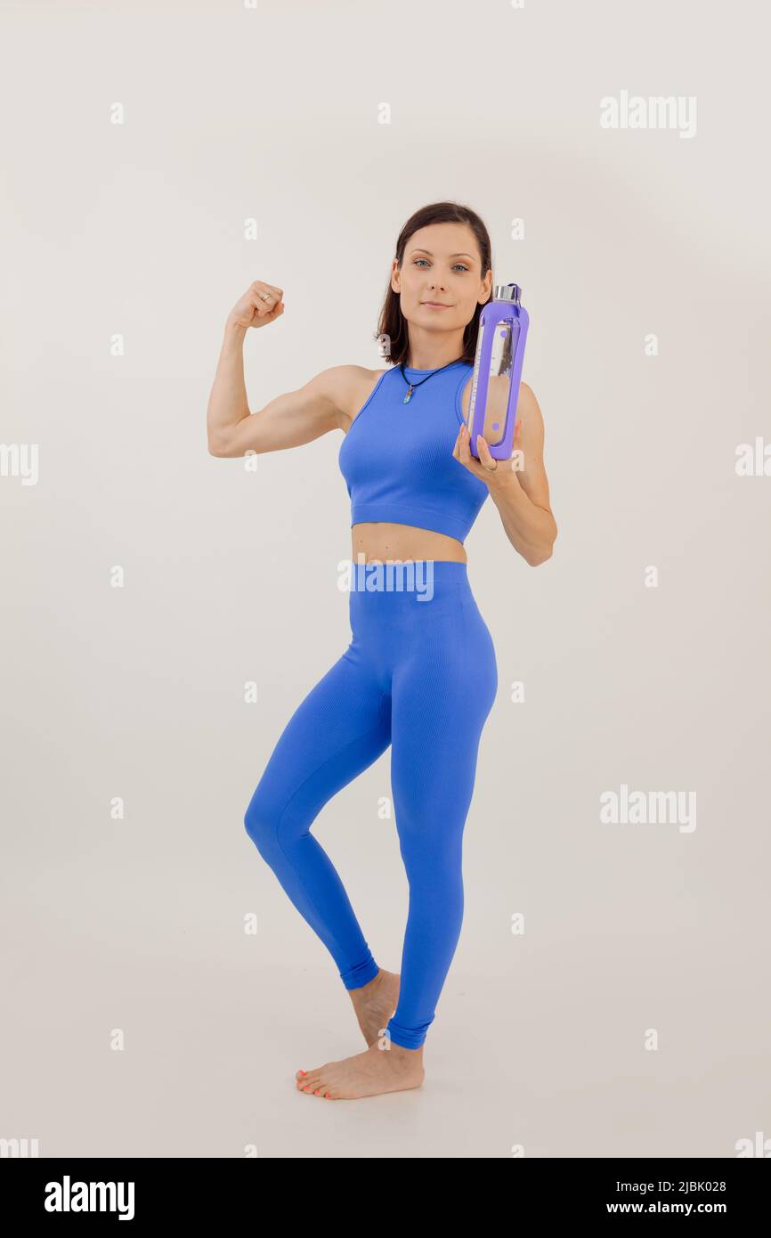Young athletic woman in blue fitness suit standing with bottle of water ...