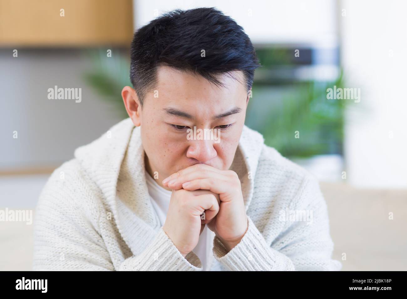 young asian man sitting on sofa at home pensive, worried about problems ...