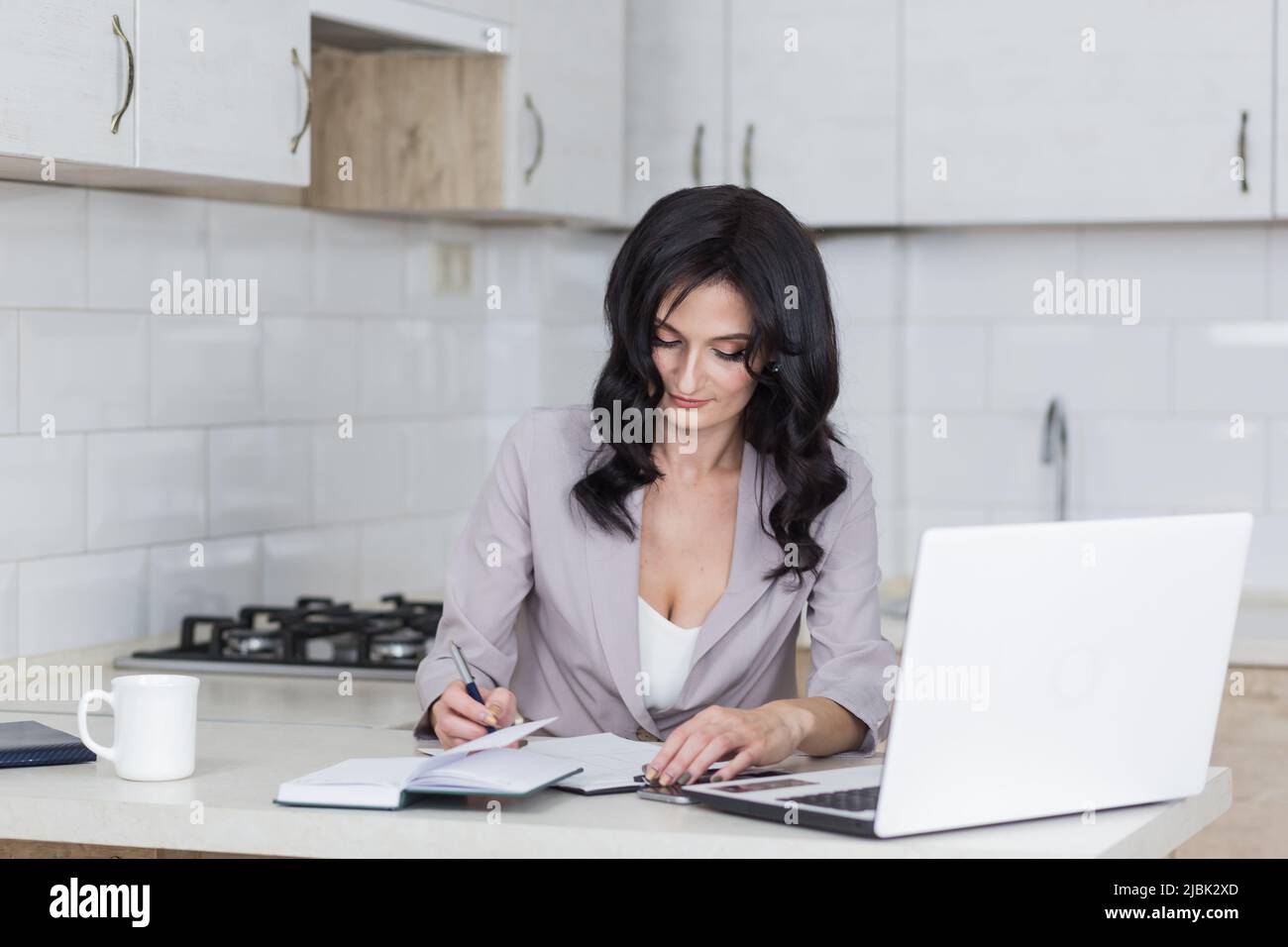 Woman working at home with with laptop, business woman in kitchen paper ...