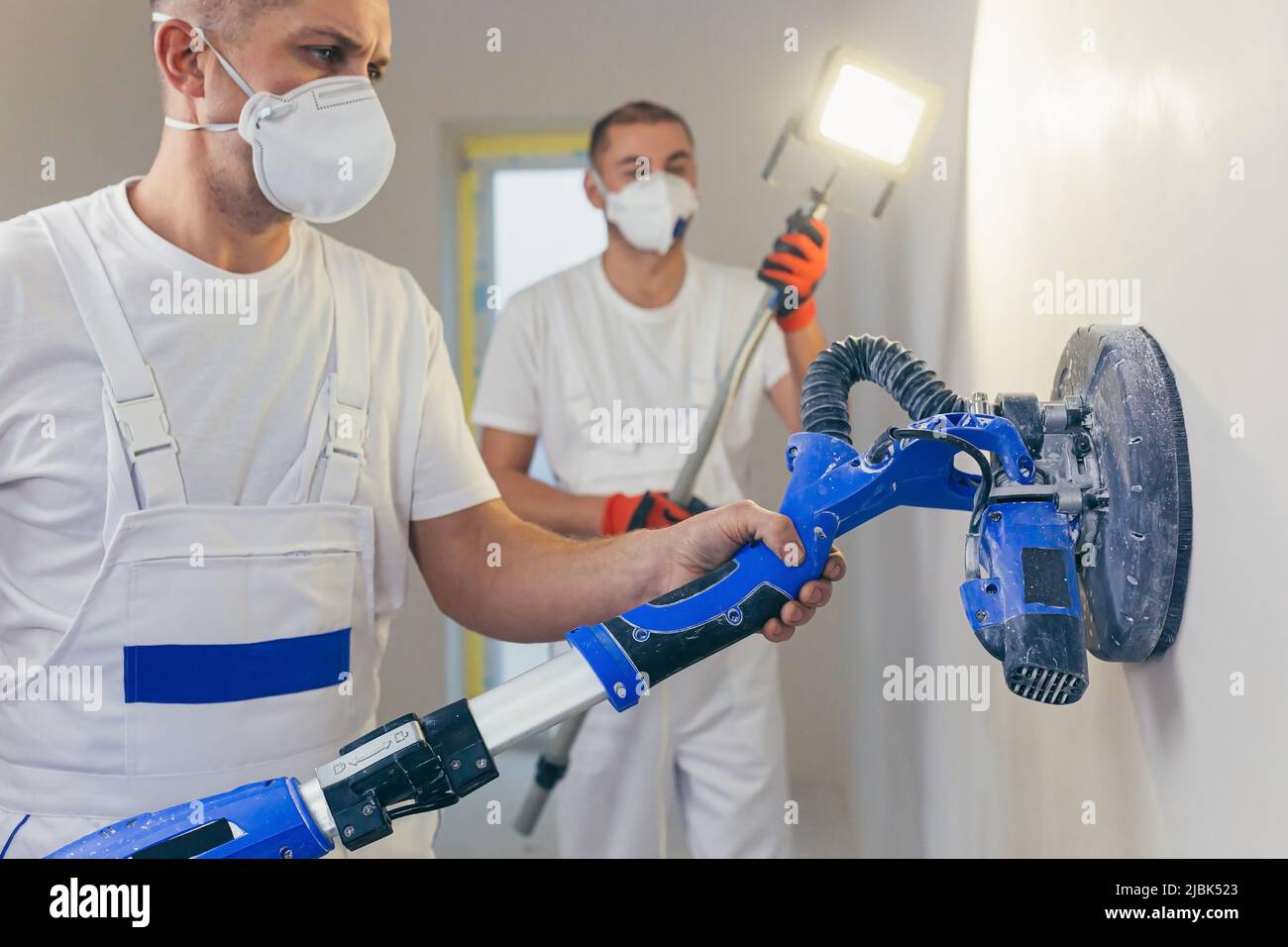 Plasterer smoothes the wall surface with a wall grinder. Two master ...