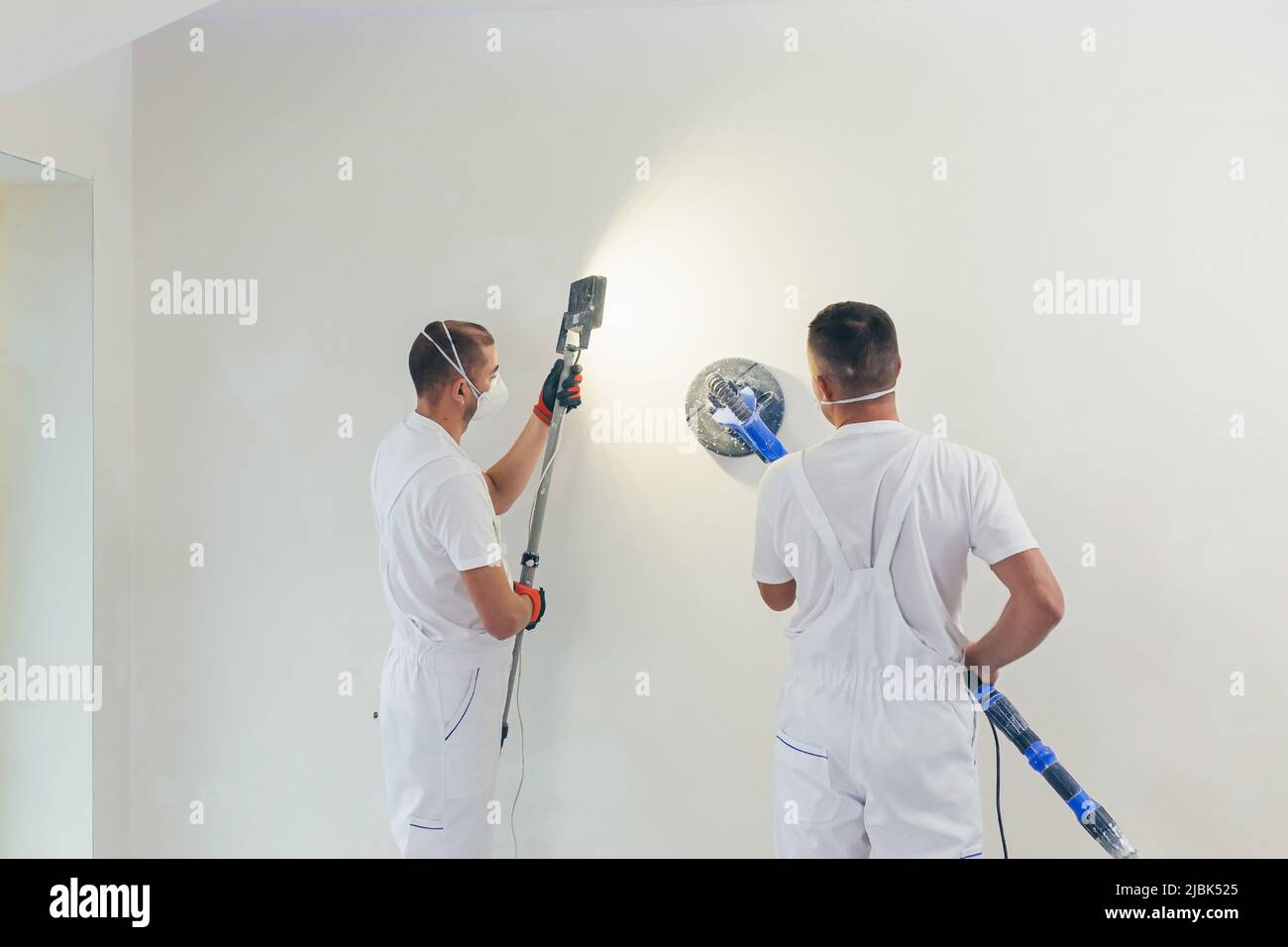 Plasterer smoothes the wall surface with a wall grinder. Two master ...