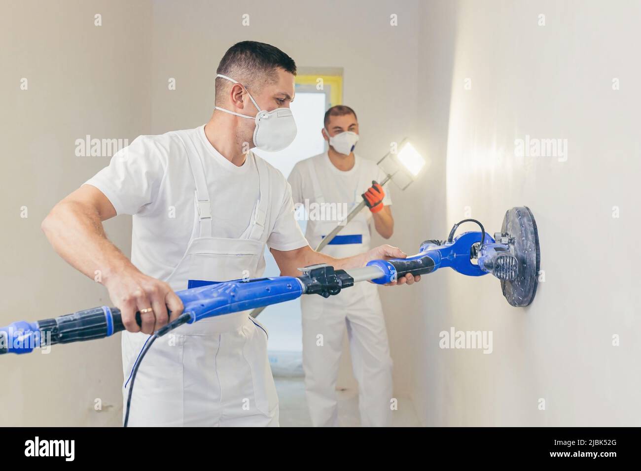 Plasterer smoothes the wall surface with a wall grinder. Two master ...