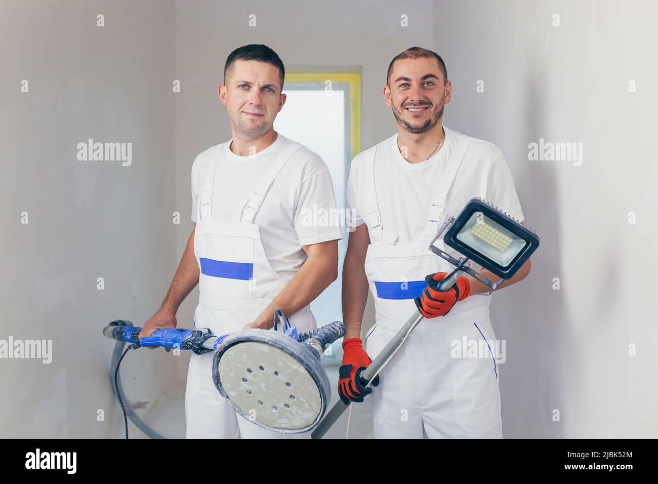 Plasterer smoothes the wall surface with a wall grinder. Two master ...