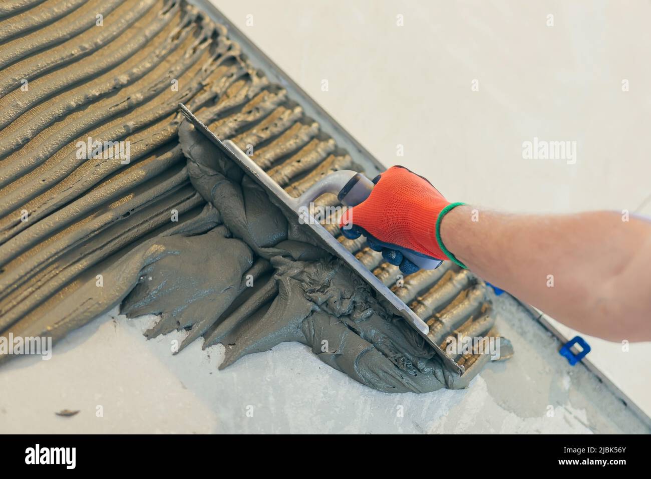Close up of the hands of a master builder's man with a notched trowel ...