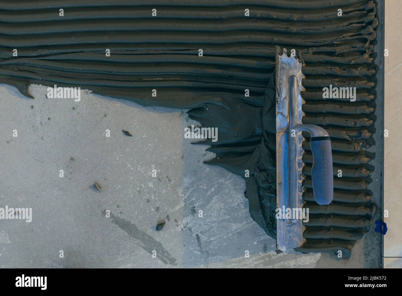 Close up of the hands of a master builder's man with a notched trowel ...
