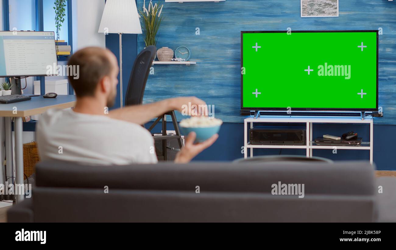 Man relaxing on couch looking at green screen on tv watching movie ...