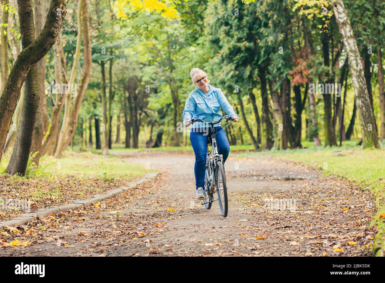 Senior beautiful blonde woman rides a bike in the park, in the woods ...