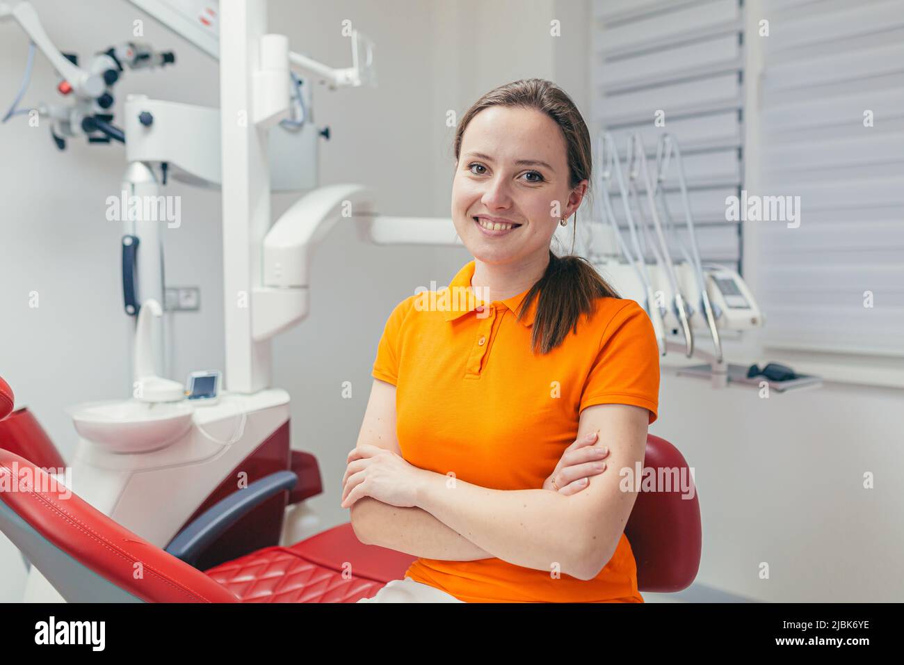 Portrait of a young beautiful female dentist, assistant in orange ...