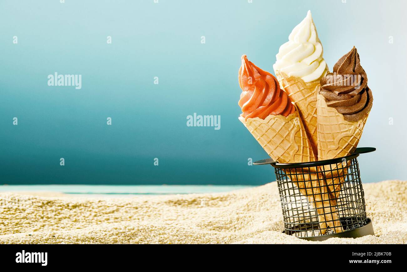 Three crunchy wafer cones with ice cream stuck in container on sandy ...