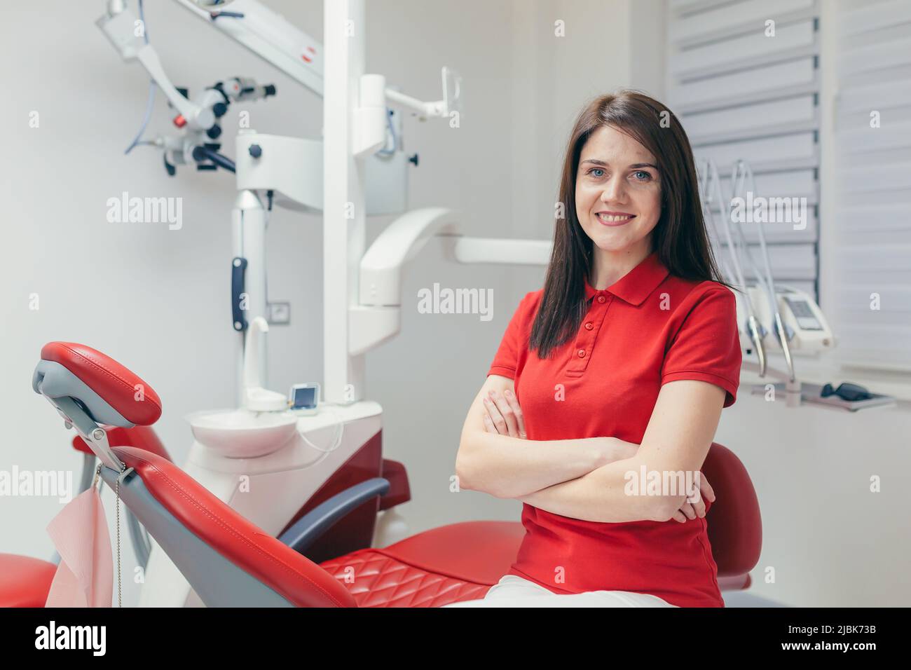 Portrait of a young beautiful female dentist, assistant in a red ...