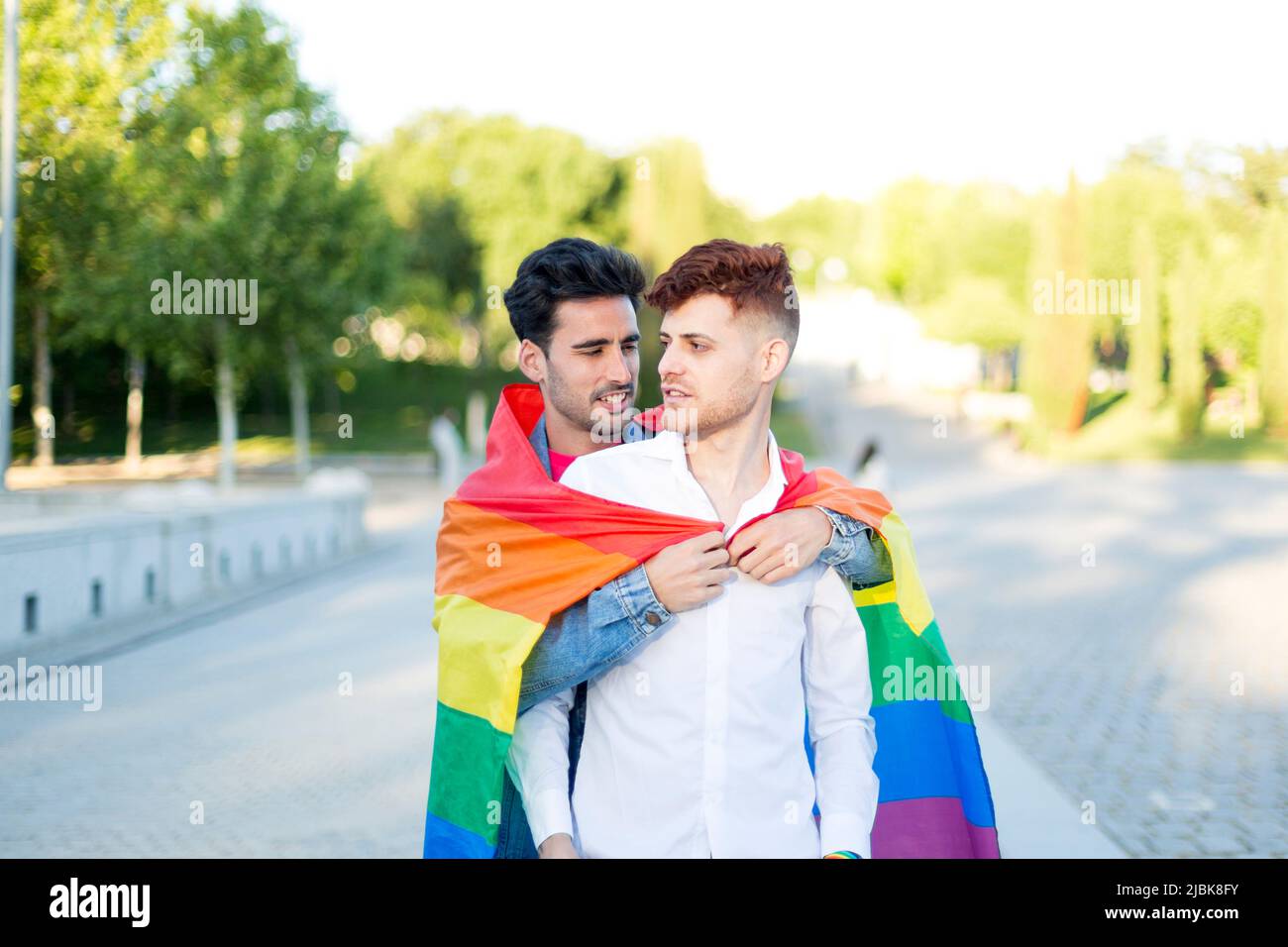 two homosexual men embracing and covered with a LGBT Pride flag looking ...