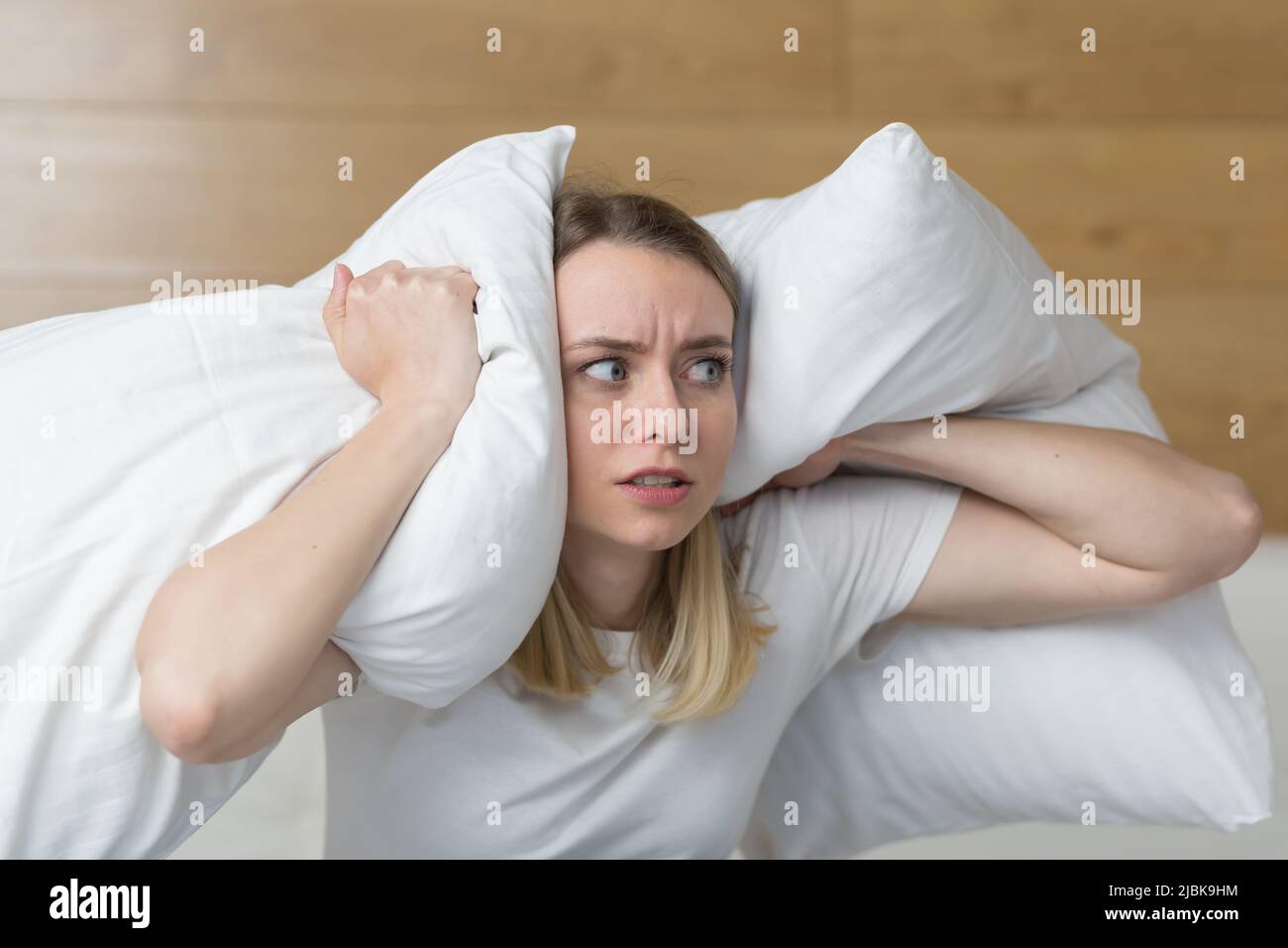 Angry young woman sitting on the bed at home, in a hotel room, covers ...
