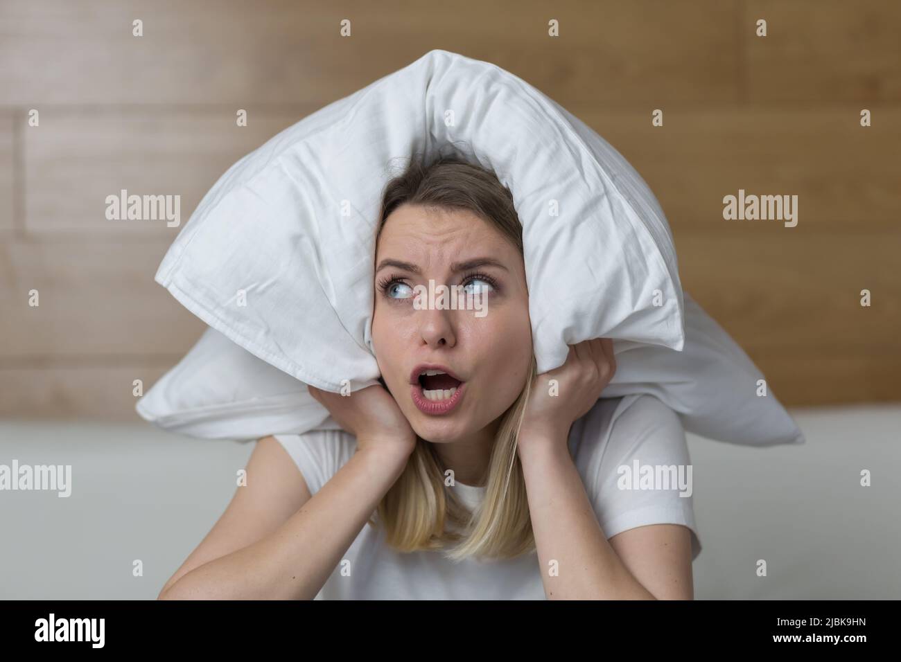 Angry young woman sitting on the bed at home, in a hotel room, covers ...