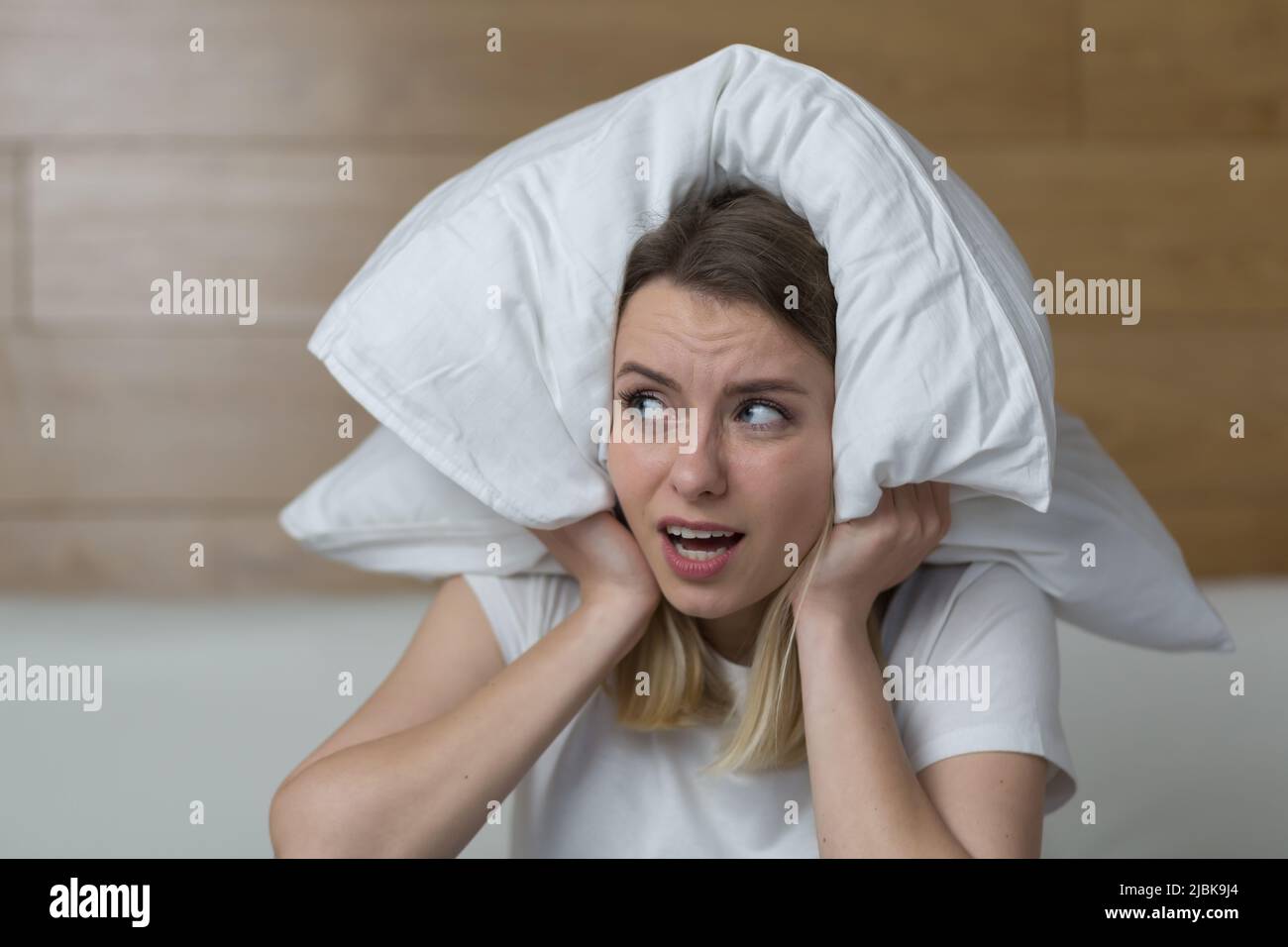 Angry young woman sitting on the bed at home, in a hotel room, covers ...