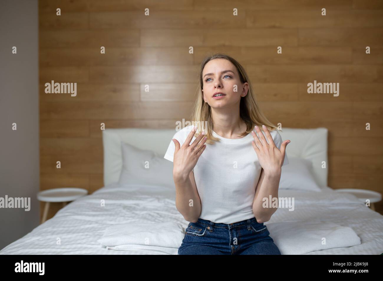 Young woman sitting on bed at home, feeling bad, panic attack, waving ...