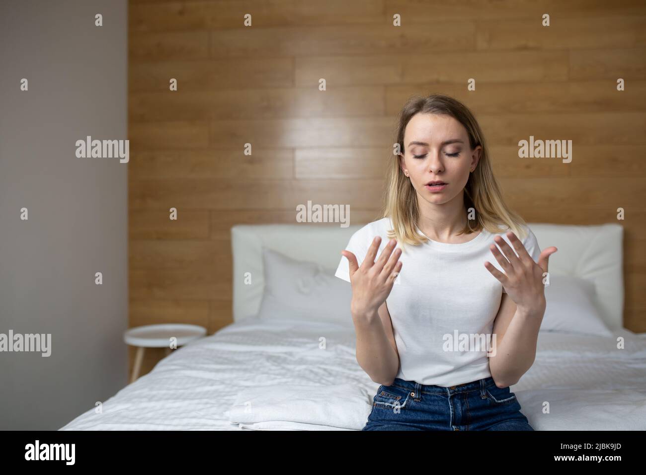 Young woman sitting on bed at home, feeling bad, panic attack, waving ...