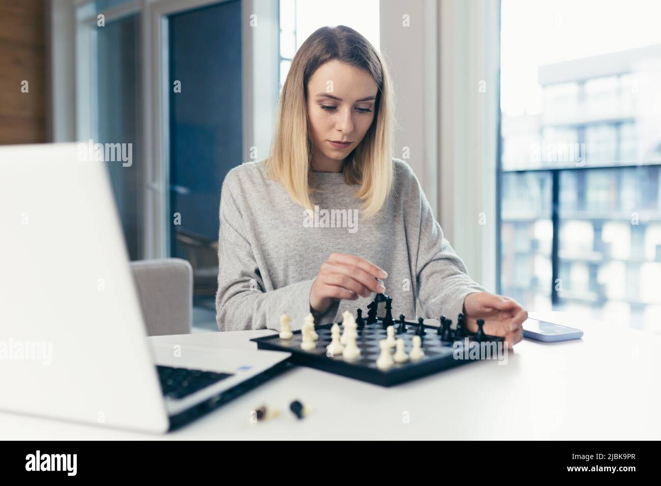 Portrait of young beautiful woman playing chess online via laptop at ...