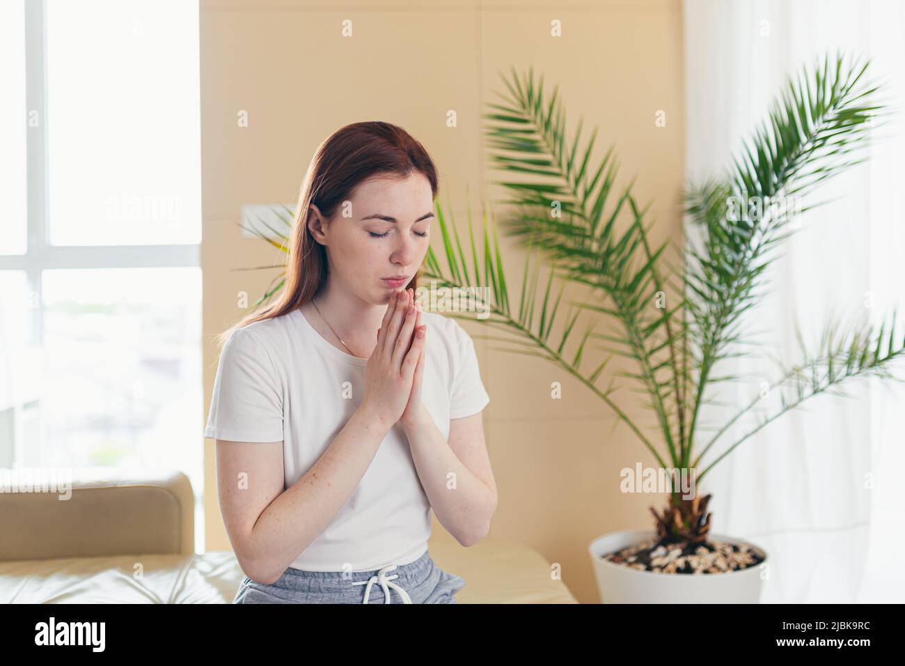Closeup portrait of a young woman praying sincerely with folded arms at ...