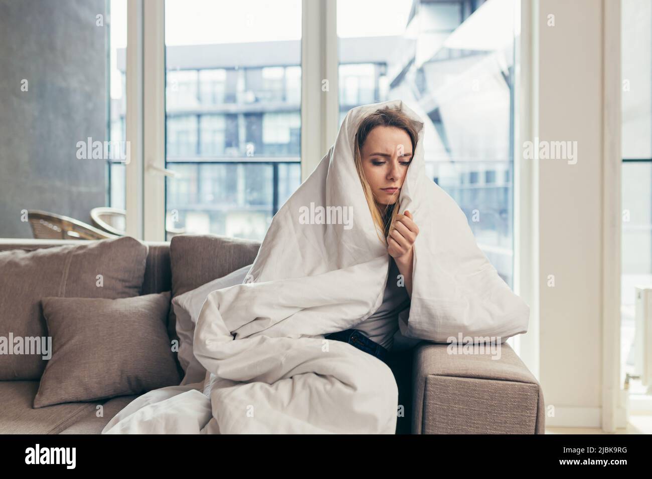 Young woman covered with a blanket sitting on the couch at home sick ...