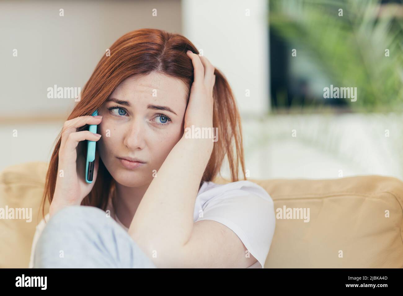 Young beautiful woman sitting alone at home on the couch, feeling pain ...