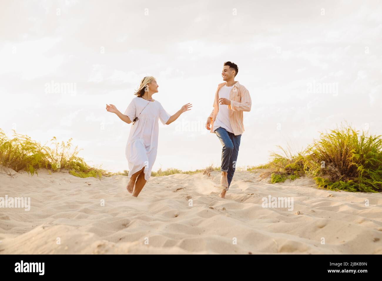 Multiracial young couple smiling while running on summer beach Stock ...