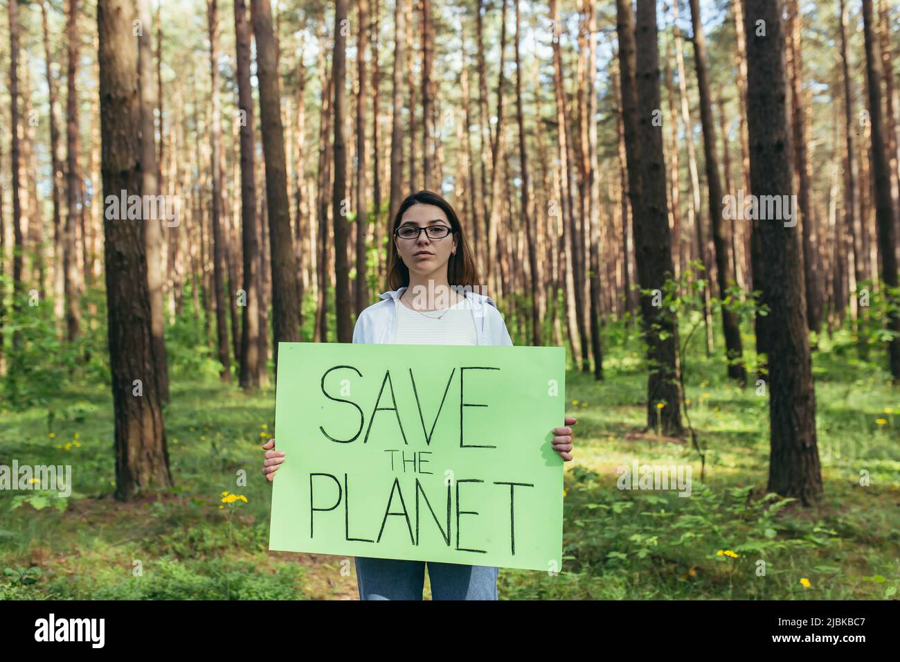 Young female activist standing in the woods with a poster save the ...