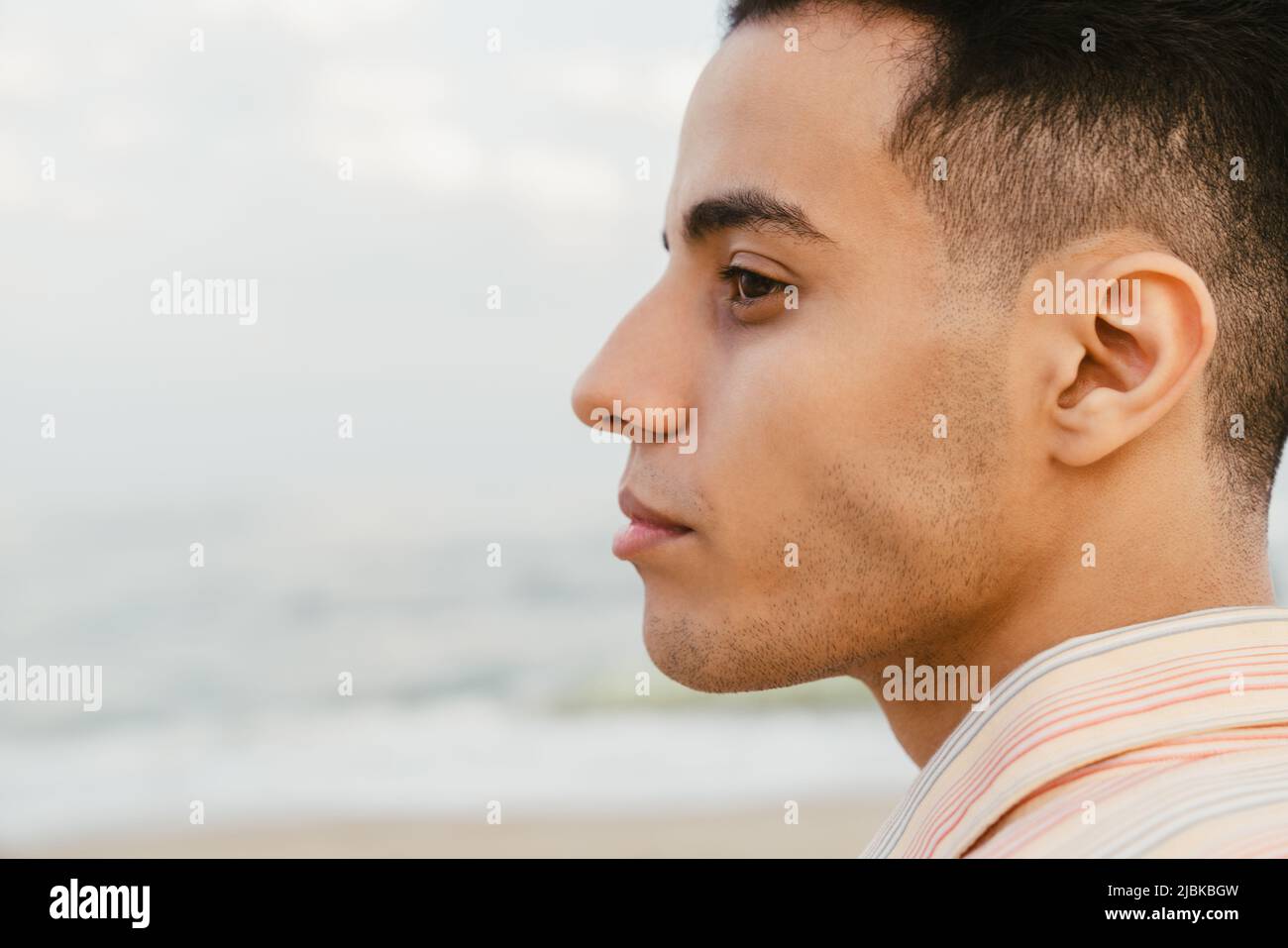 Young middle eastern man looking aside during walking on summer beach ...