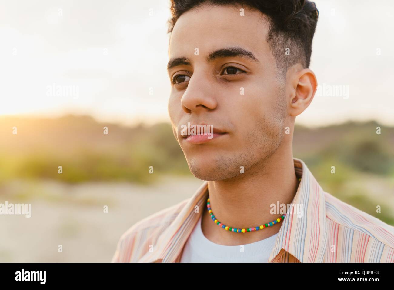 Young middle eastern man looking aside during walking on summer beach ...