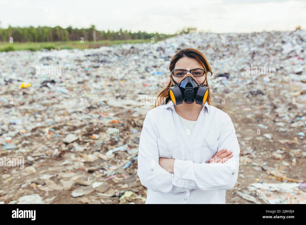 Female scientist in a protective respirator mask at a landfill assesses ...