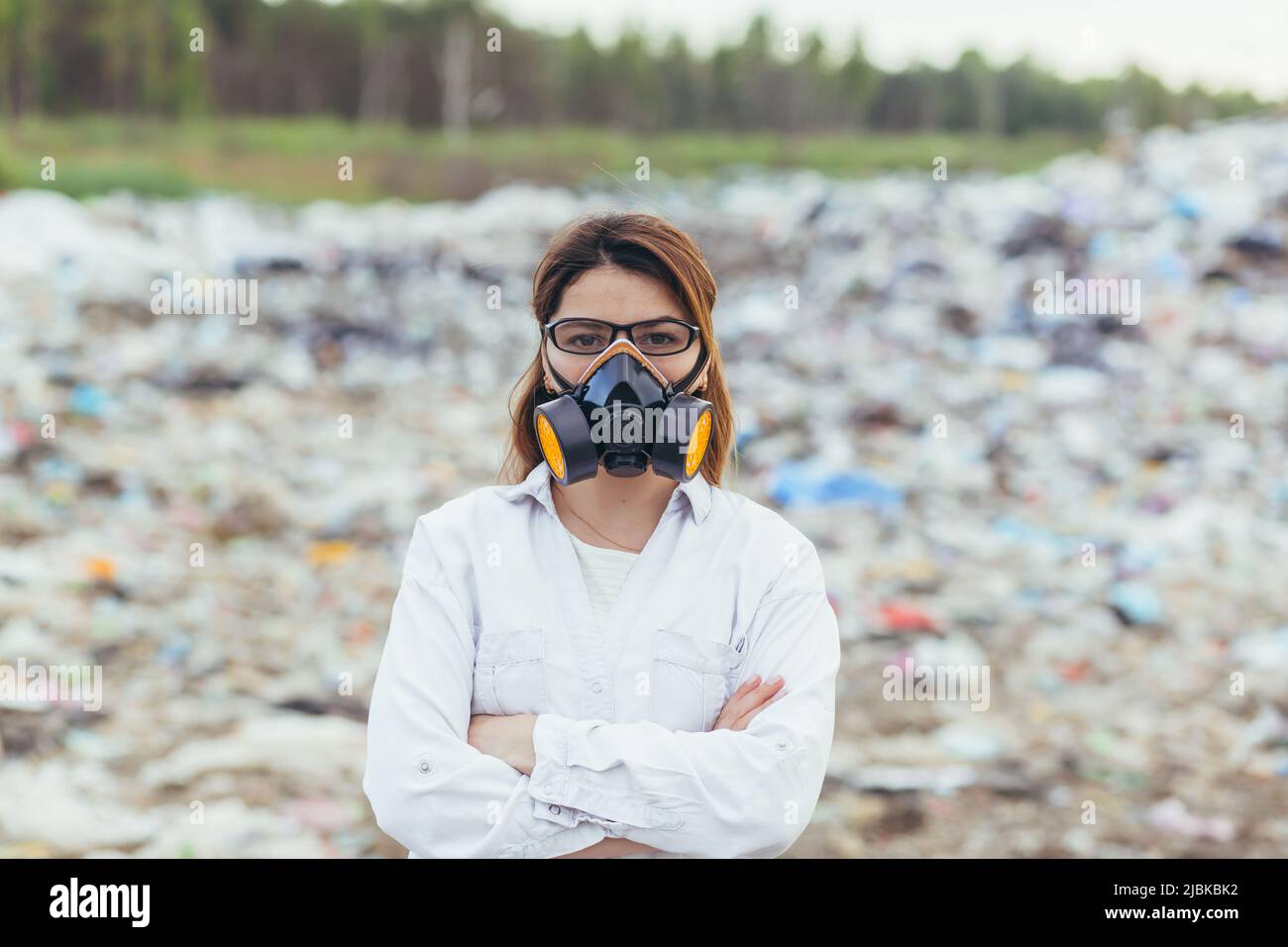 Female scientist in a protective respirator mask at a landfill assesses ...