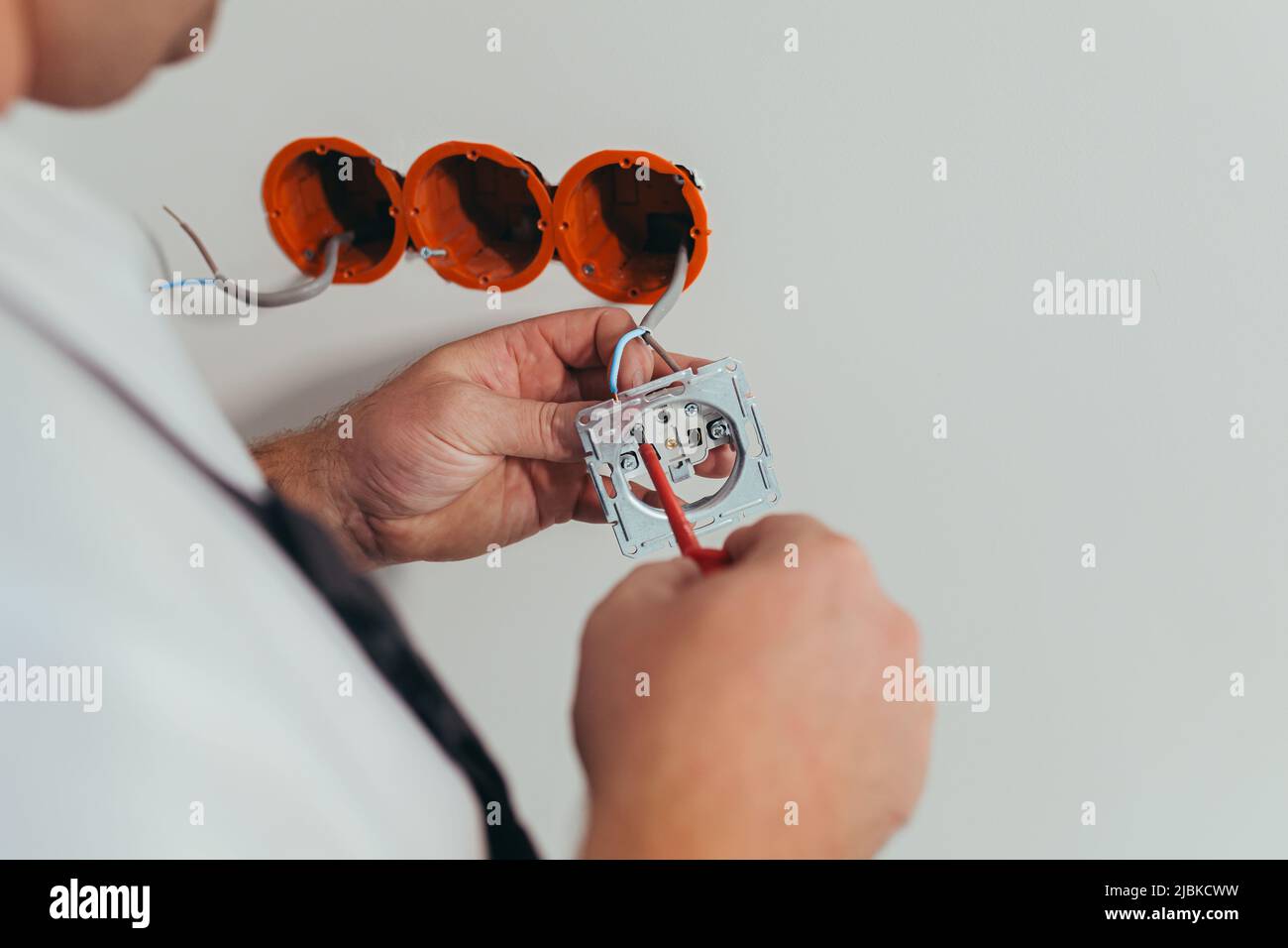 Male worker professional electrician mounts an electrical outlet in the ...