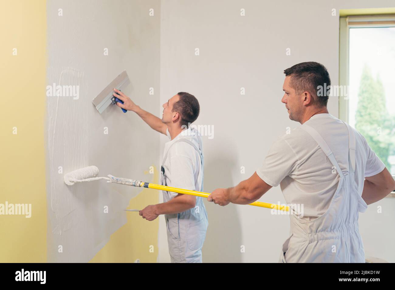Two men apply plaster to the wall and repair the house Stock Photo - Alamy