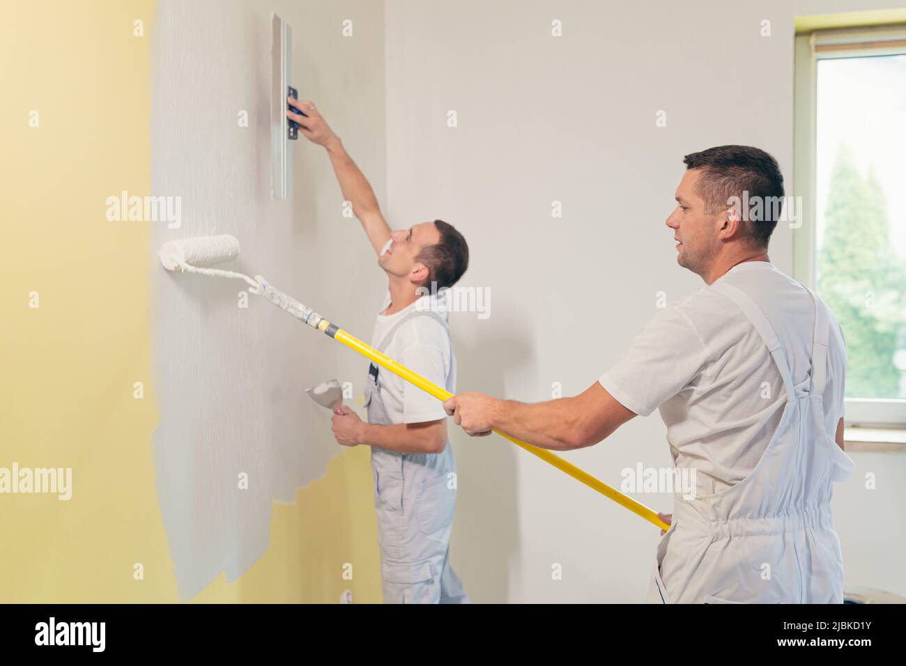 Two men apply plaster to the wall and repair the house Stock Photo - Alamy