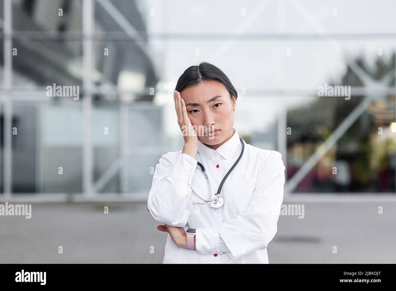 Young asian doctor woman in white medical gown near clinic, tired ...