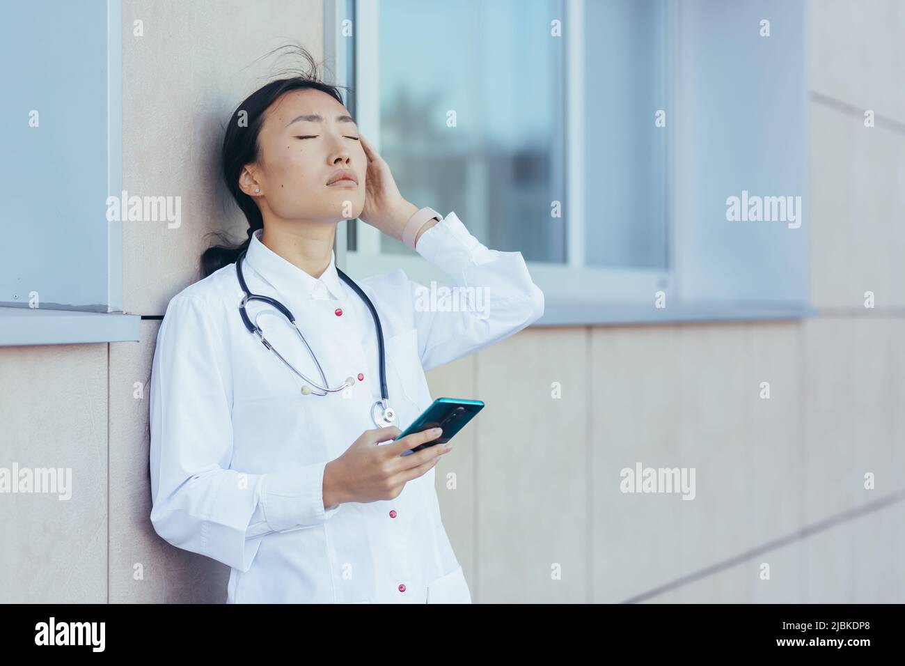 Sad doctor nurse Asian, near the clinic during a break, uses the phone ...