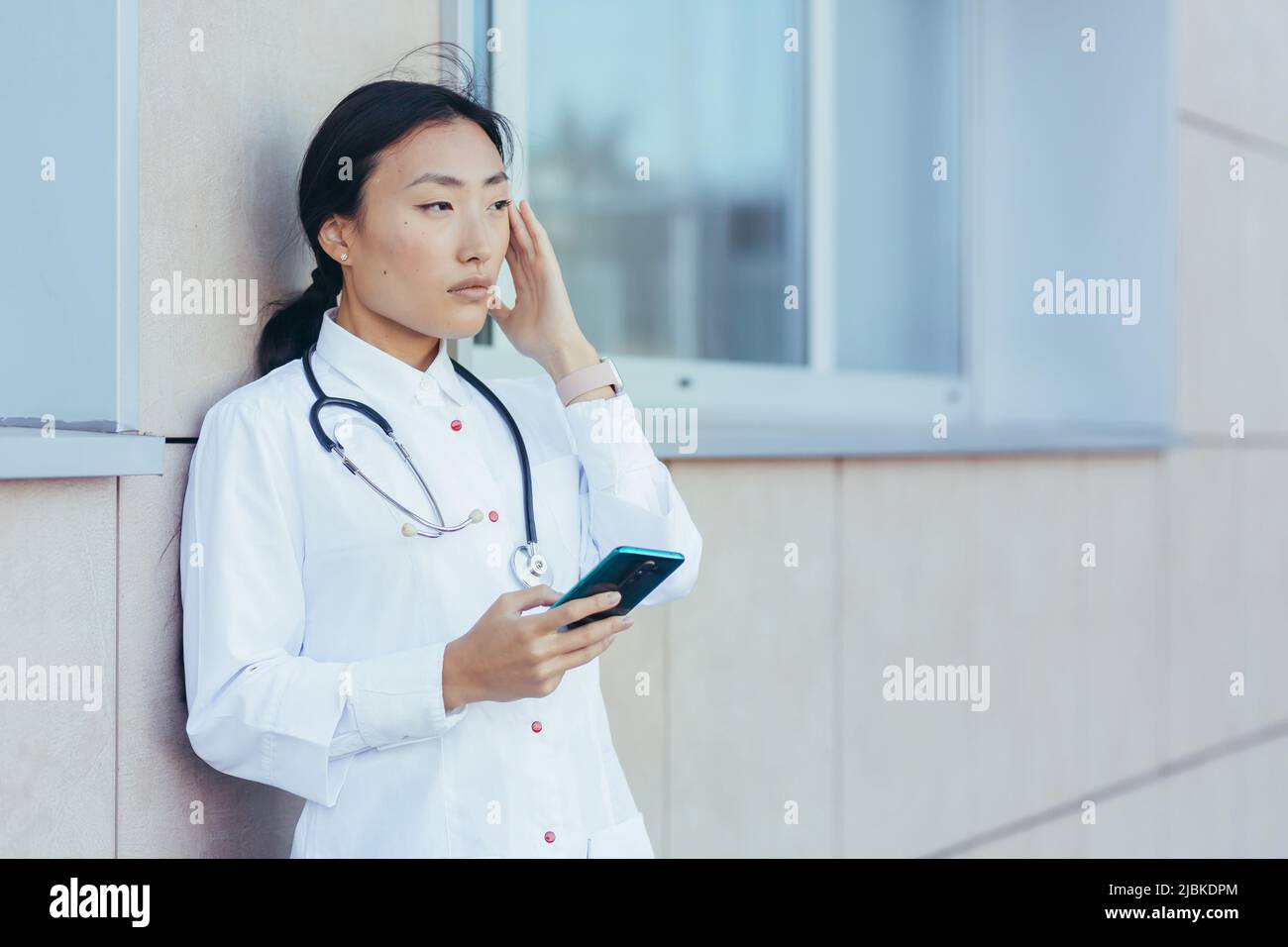 Sad doctor nurse Asian, near the clinic during a break, uses the phone ...