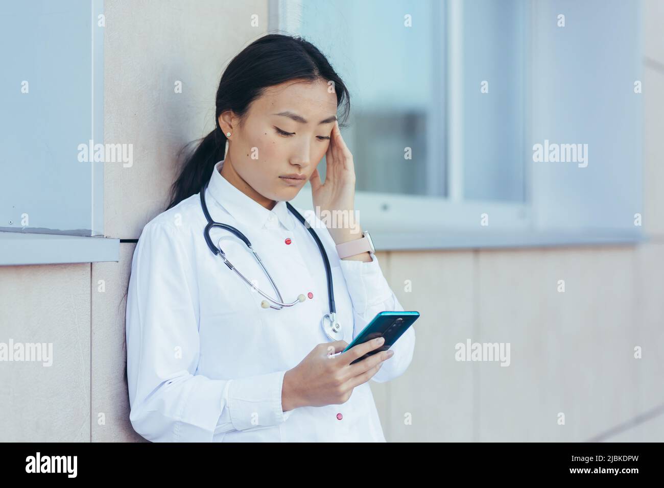 Sad doctor nurse Asian, near the clinic during a break, uses the phone ...