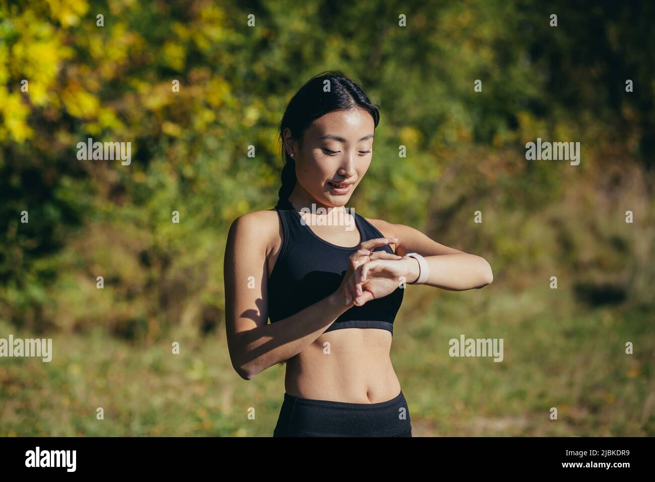 Sporty asian woman looking smart watch at modern track runner using use ...