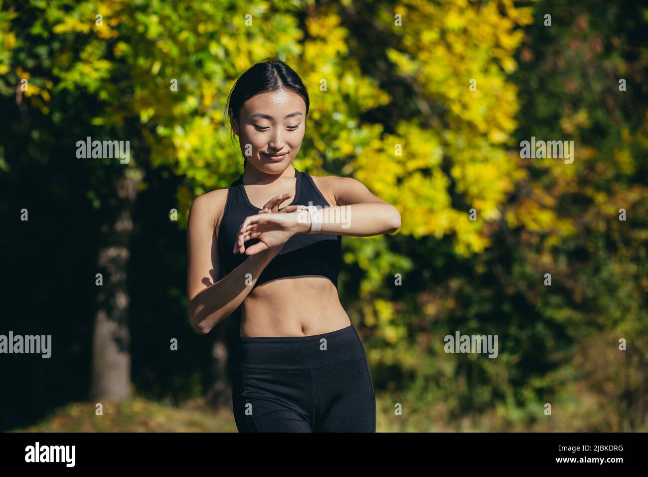 Sporty asian woman looking smart watch at modern track runner using use ...