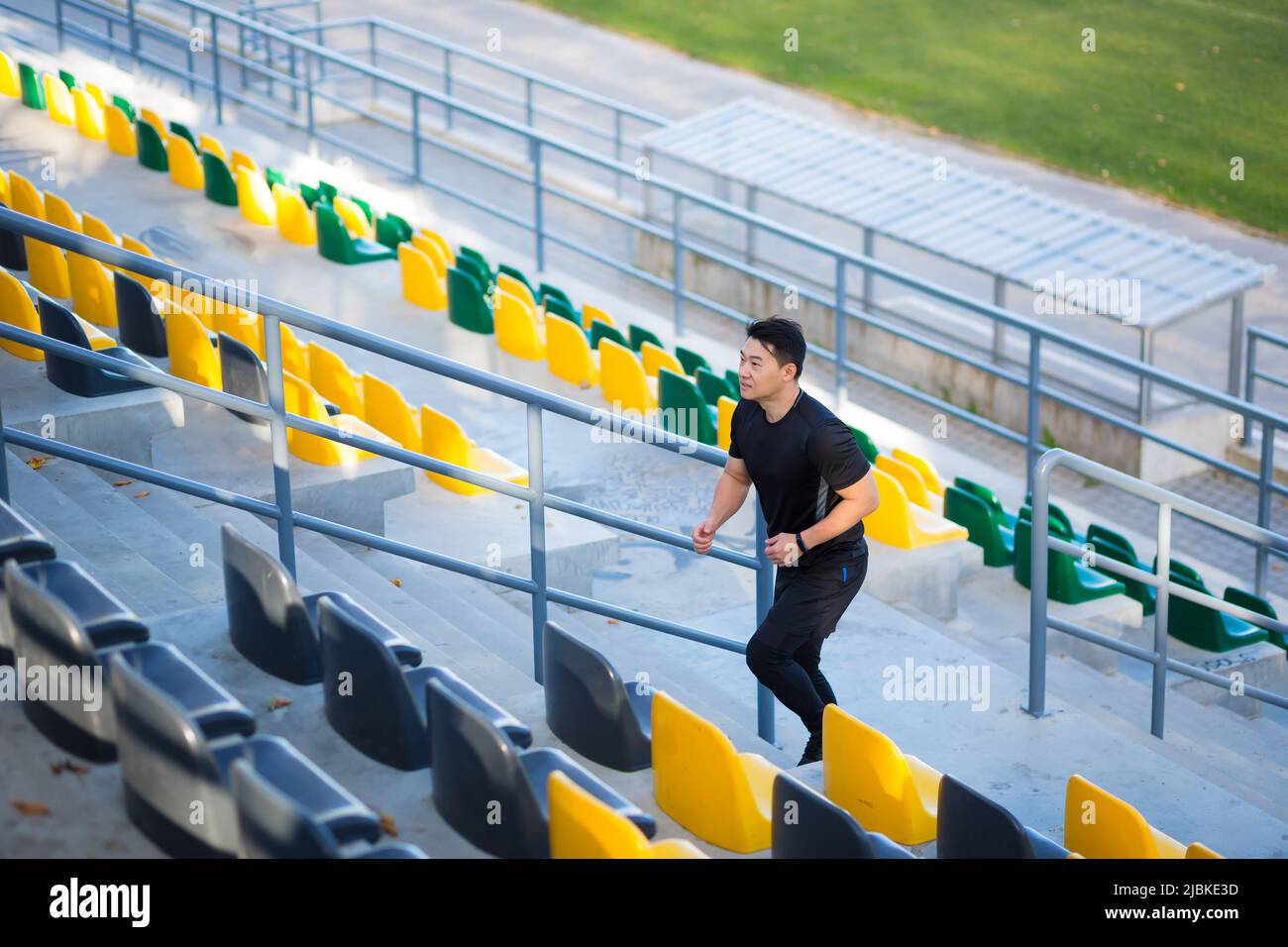 Asian male runner running around modern urban stadium up stairs Cardio ...