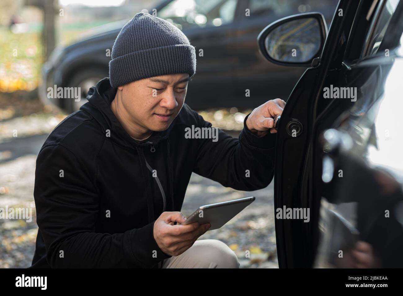 male bandit thief car thief asian uses a tablet to turn off the car ...