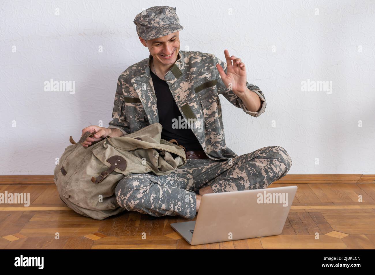 Happy army soldier having video call over laptop and waving to someone ...