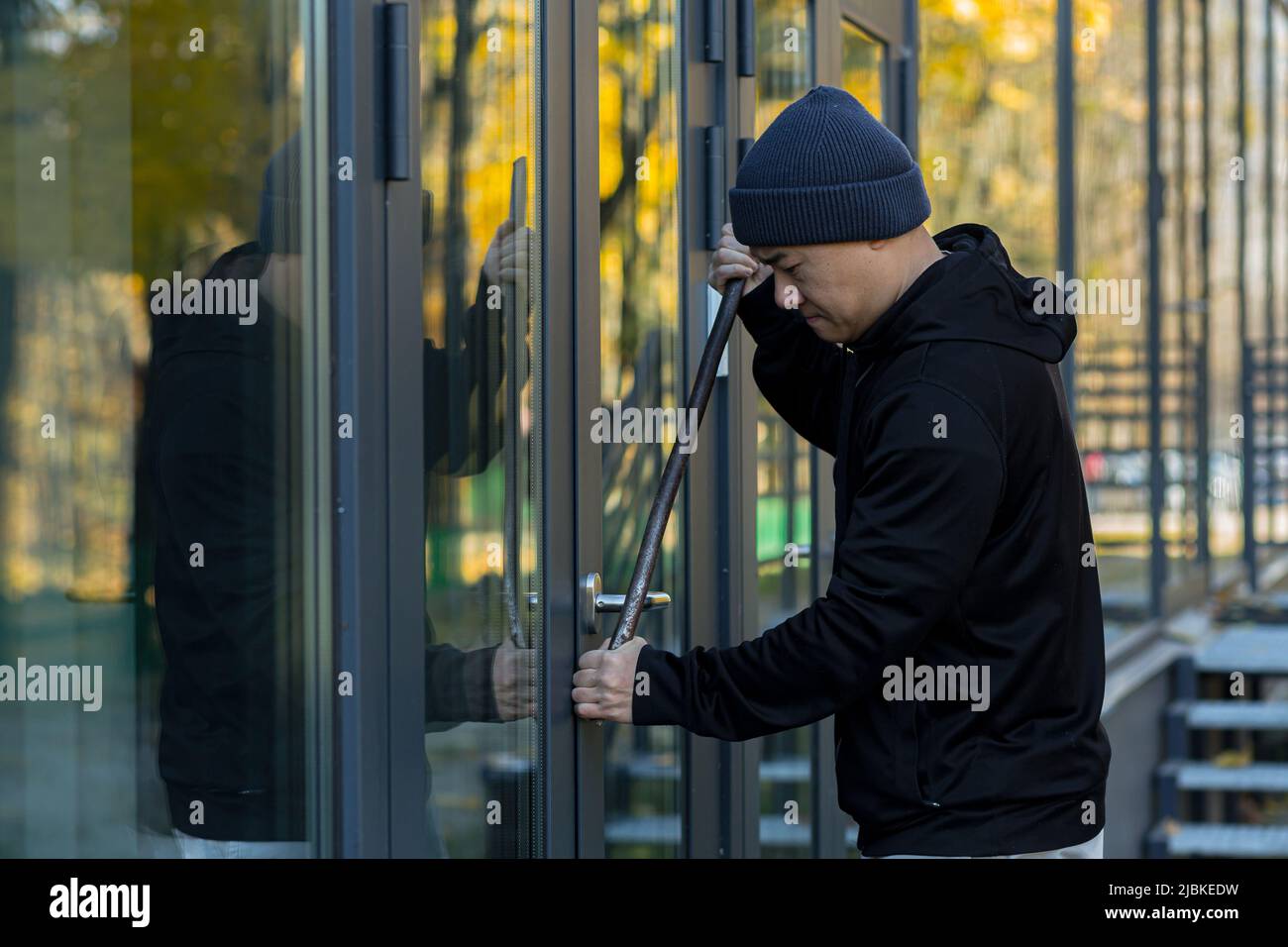Asian man robber tries to break the door lock with a large metal ...